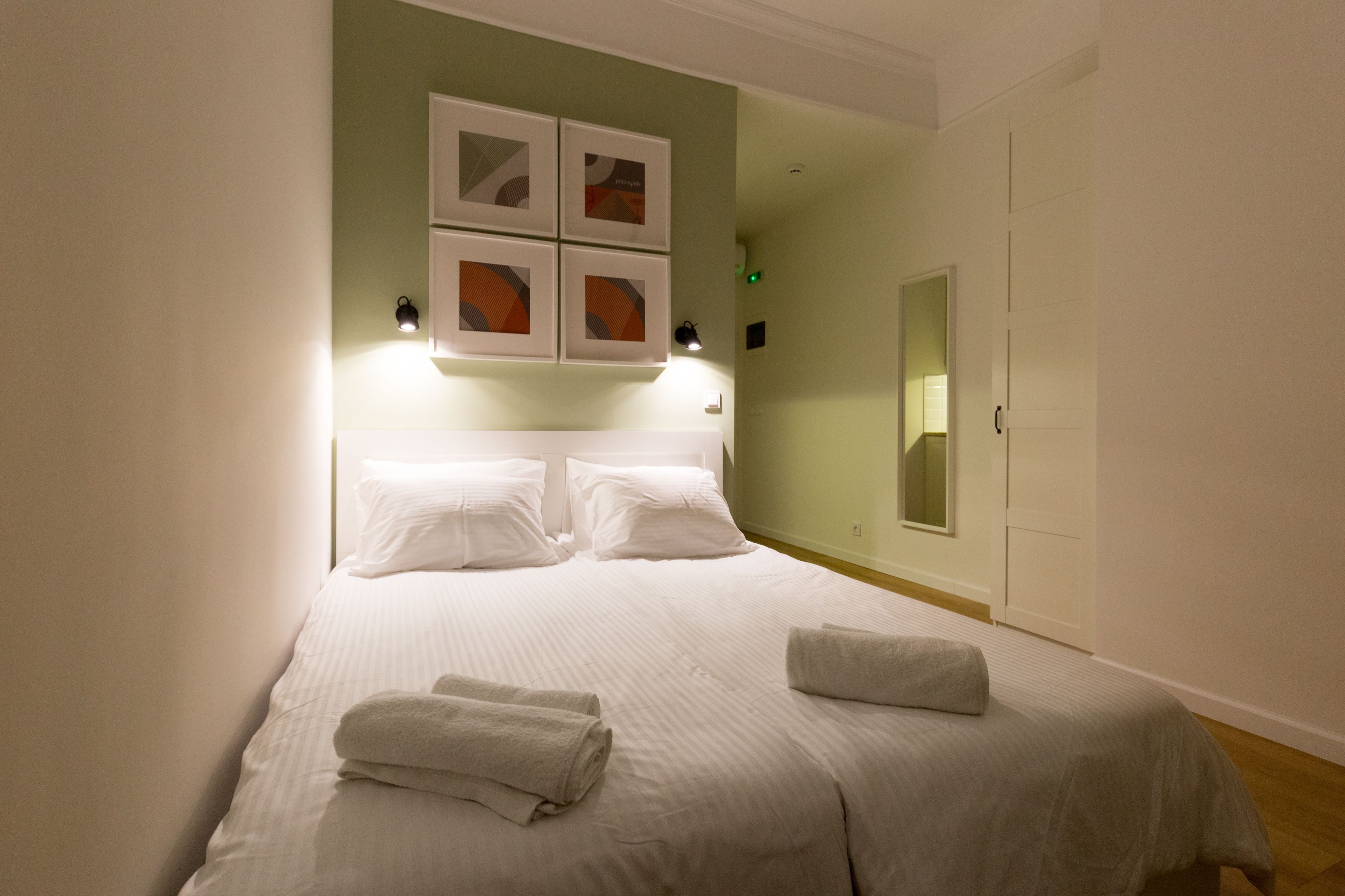 Uma cama bem arrumada com lenç óis brancos e duas almofadas, um abajur e um quadro pendurado na parede.