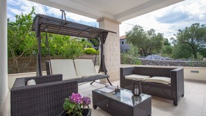 Um pátio externo com móveis de vime, uma mesa de centro de vidro e uma pérgula.