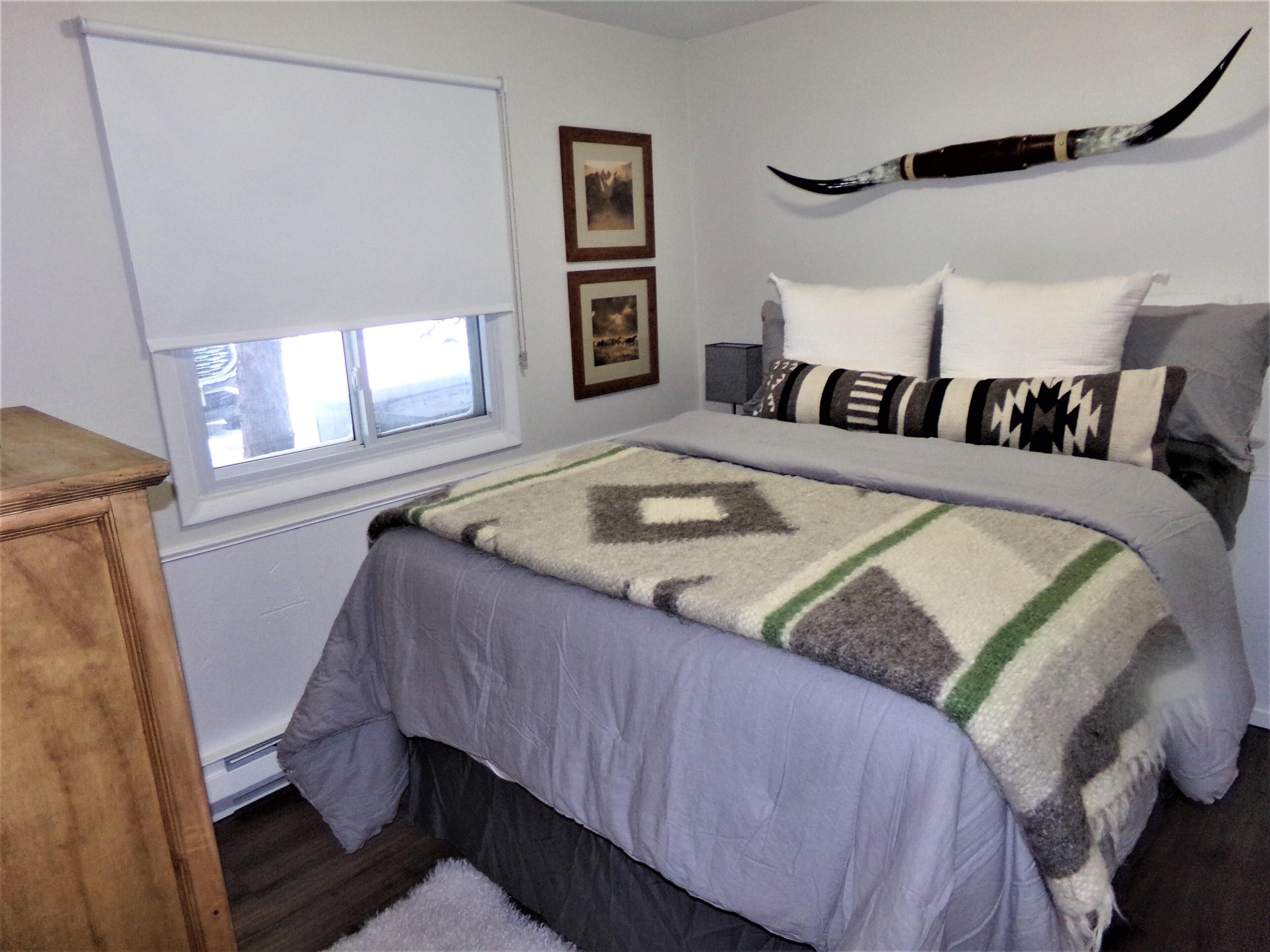 Quarto com cama, janela, moldura de quadro e um chifre de animal fixado na parede.