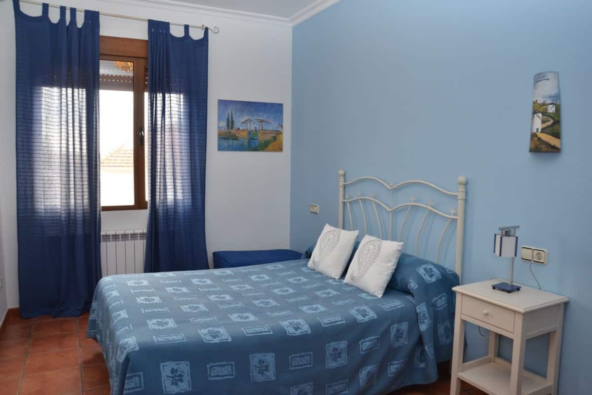 Quarto com uma cama, mesa de cabeceira e janela com cortinas.