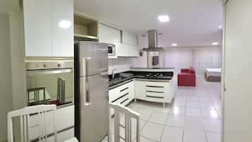 Cozinha moderna com geladeira, fogão e micro-ondas. Há uma mesa de jantar com cadeiras e um sofá vermelho na sala de estar.