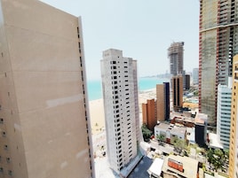 Um edifício alto com fachada em grade, vista para a praia e outros edifícios ao redor.
