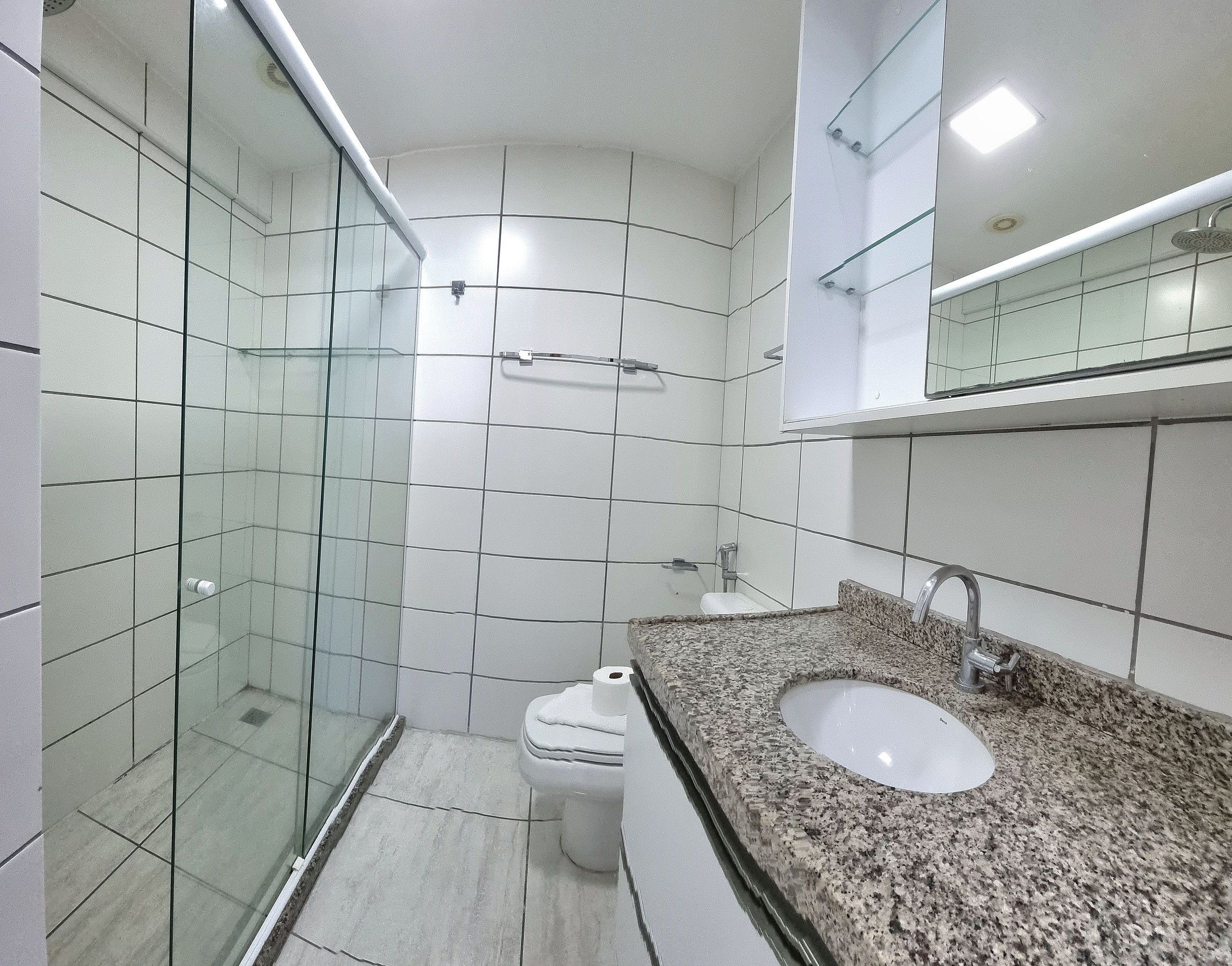 Casa de banho com cabine de duche em vidro, sanita e lavatório com bancada de granito.