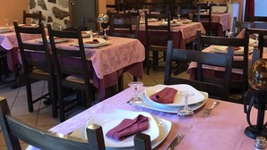 Restaurante com paredes de pedra, vigas de madeira e mesas dispostas com pratos, copos e guardanapos.