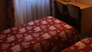 Quarto de hotel com duas camas, uma escrivaninha, televisão e janela com cortinas.