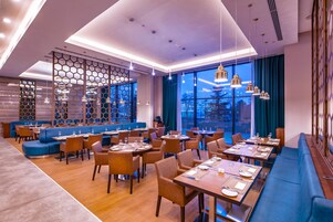 Um restaurante moderno com assentos azuis, mesas de madeira e luminárias pendentes.