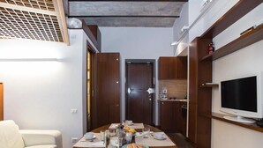 Uma sala de jantar com uma mesa redonda, sofá branco e televisão na parede.