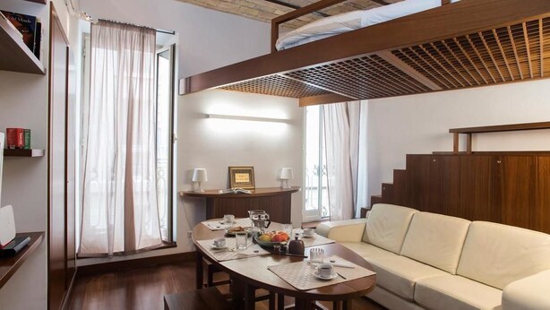 Uma sala de estar moderna com teto de madeira, um sofá, uma mesa de jantar com cadeiras e uma escada.