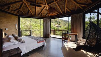 Quarto com cama grande, uma cadeira suspensa e vista para o exterior.