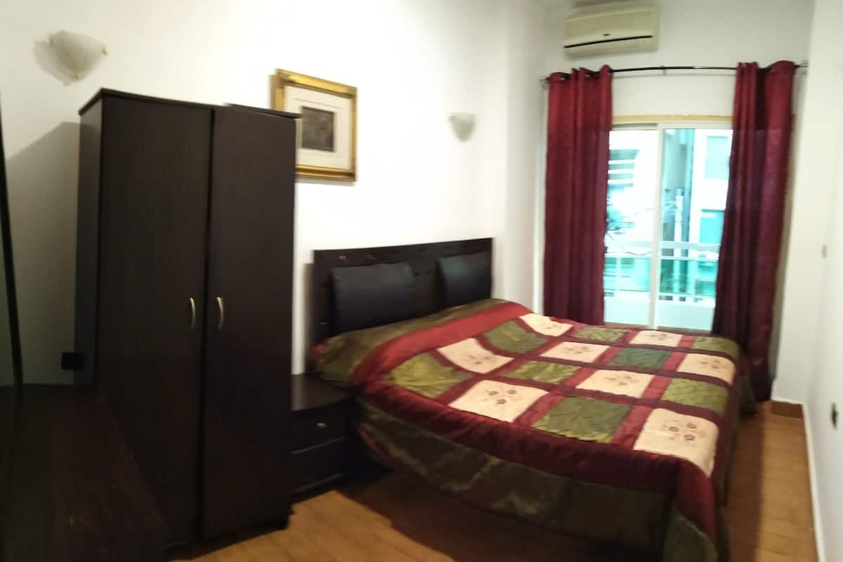Quarto com cama, guarda-roupa, um quadro na parede e janela com cortinas.