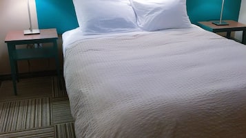 Cama bem arrumada com lençóis brancos, duas mesas de cabeceira com luminárias e um tapete estampado.