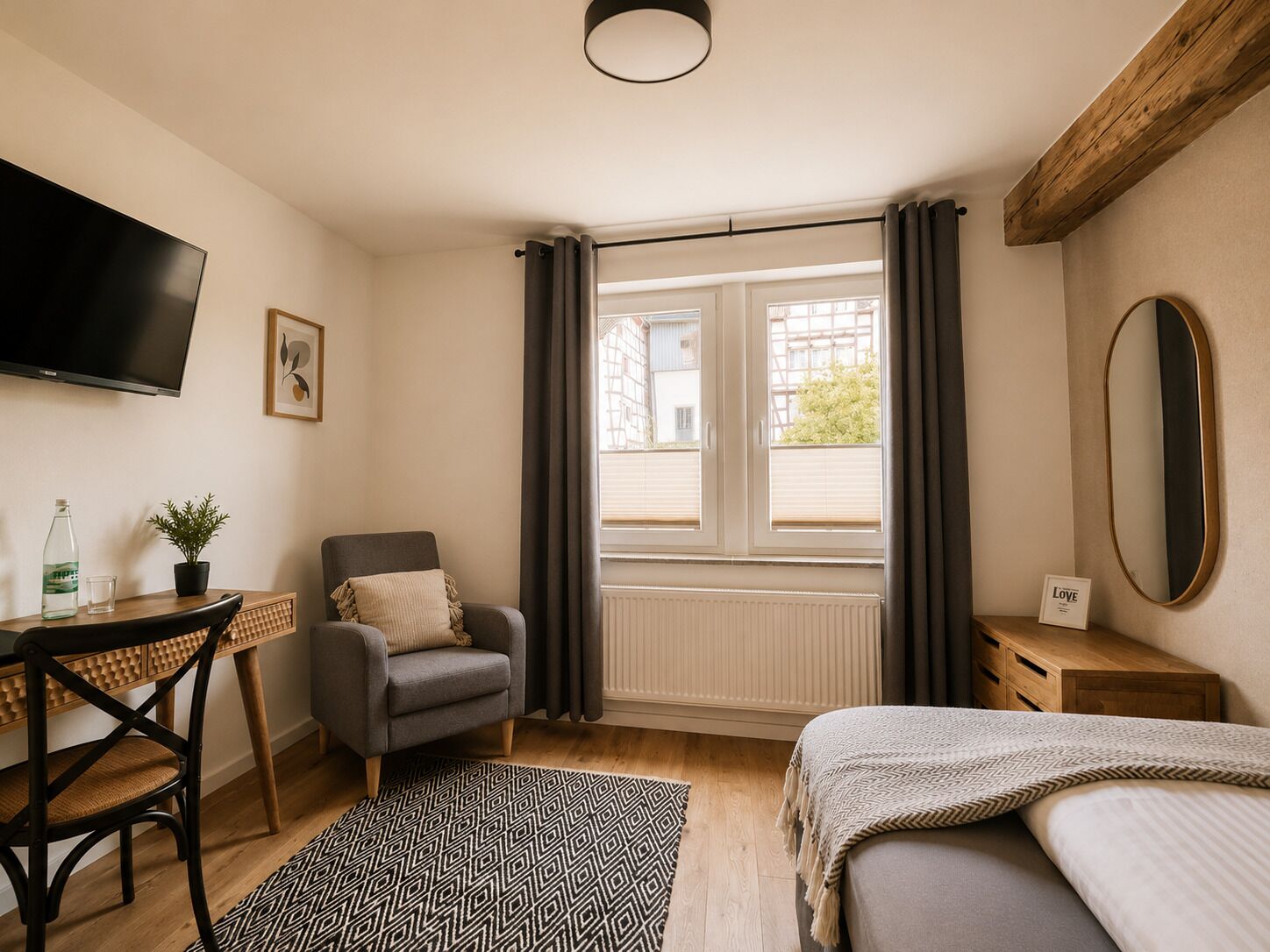 Quarto com cama, escrivaninha, cadeira, televisão, janela com cortinas e radiador.