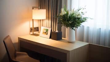 Quarto de hotel com escrivaninha, luminária, vaso com flores, moldura e caixa de lenços.