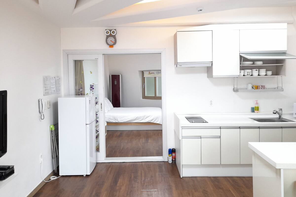 Quarto de hotel compacto com cozinha compacta, uma cama, espelho e banheiro pequeno.