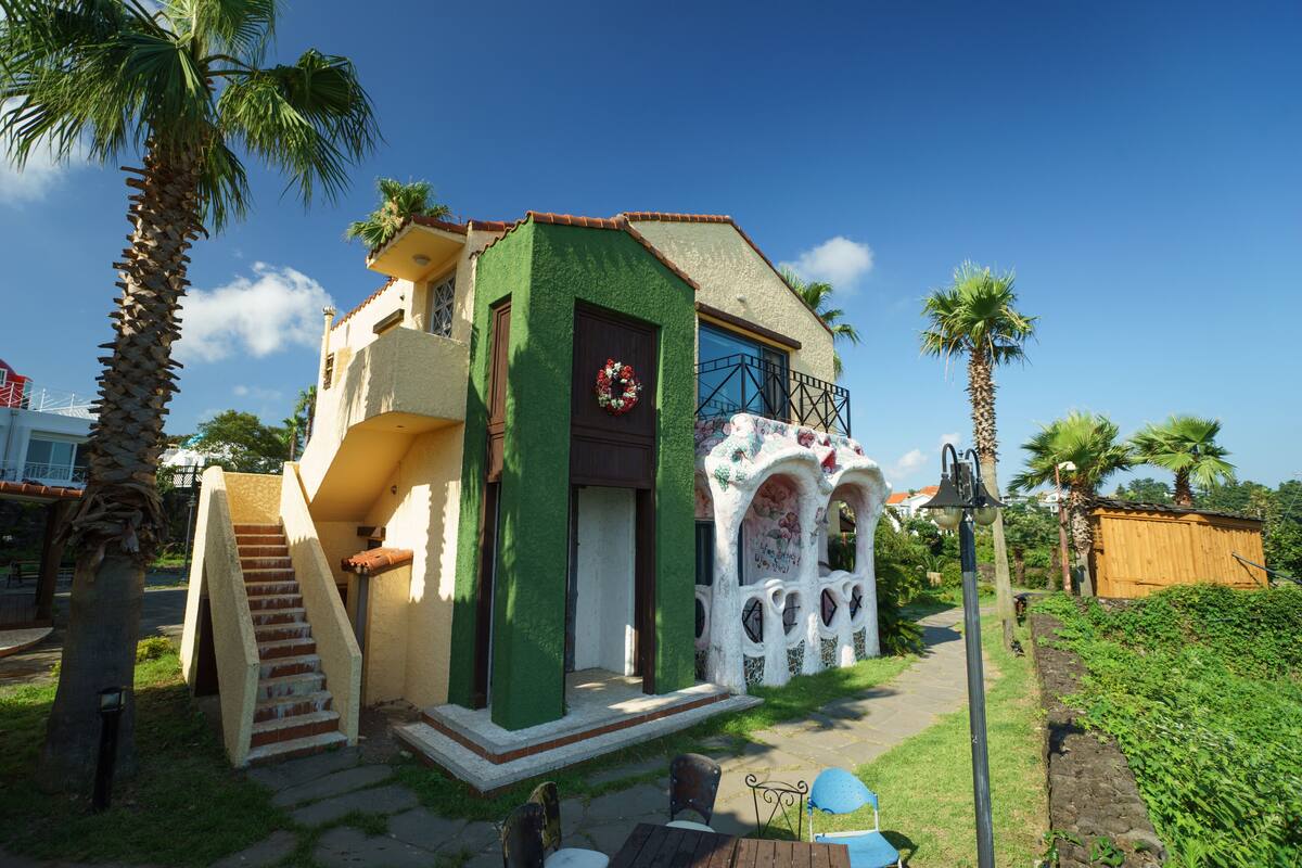 Uma casa de dois andares com fachada verde, porta de madeira e varanda.