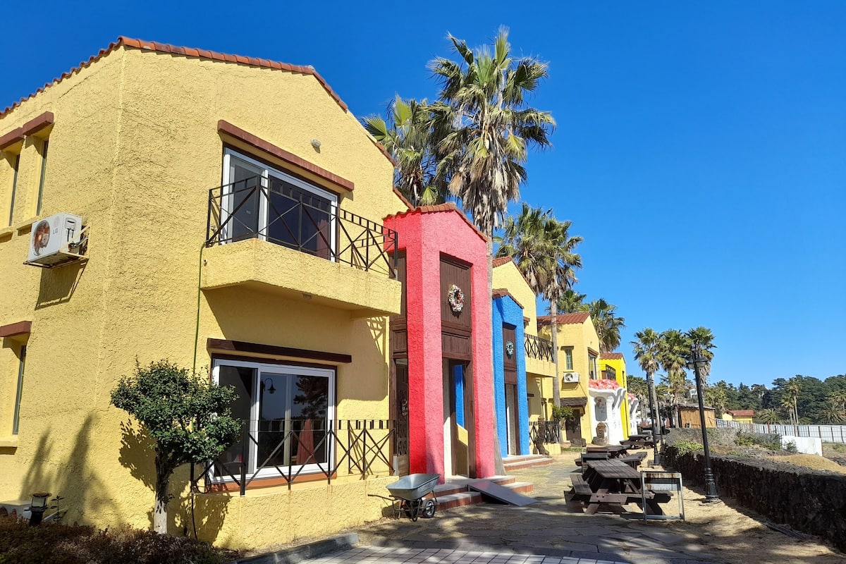 Um edifício amarelo com varanda, porta vermelha e porta azul.