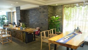 Um restaurante com uma longa mesa de madeira, cadeiras e um balcão com uma pessoa trabalhando atrás.
