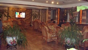 Um lobby com decoração tradicional, incluindo cadeiras de vime, plantas em vasos e uma tela de televisão.
