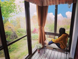 Uma pessoa sentada num banco perto de uma janela, com vista para um jardim.