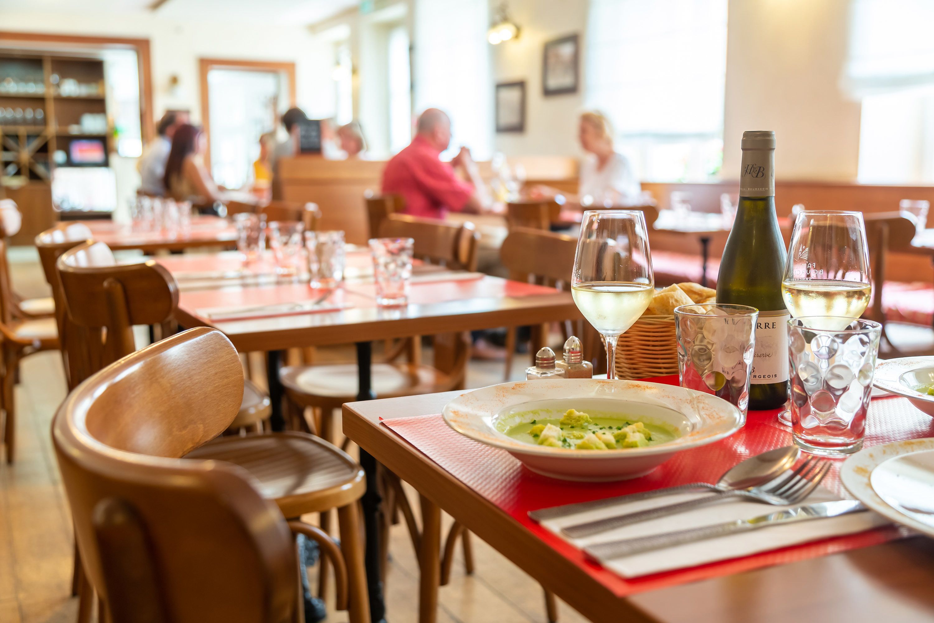 Um restaurante com mesas preparadas para refeições, copos de vinho e uma garrafa de vinho sobre a mesa.