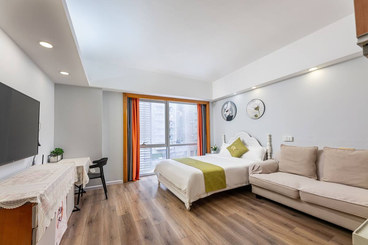 Quarto de hotel moderno com cama, sofá, escrivaninha e uma janela grande.