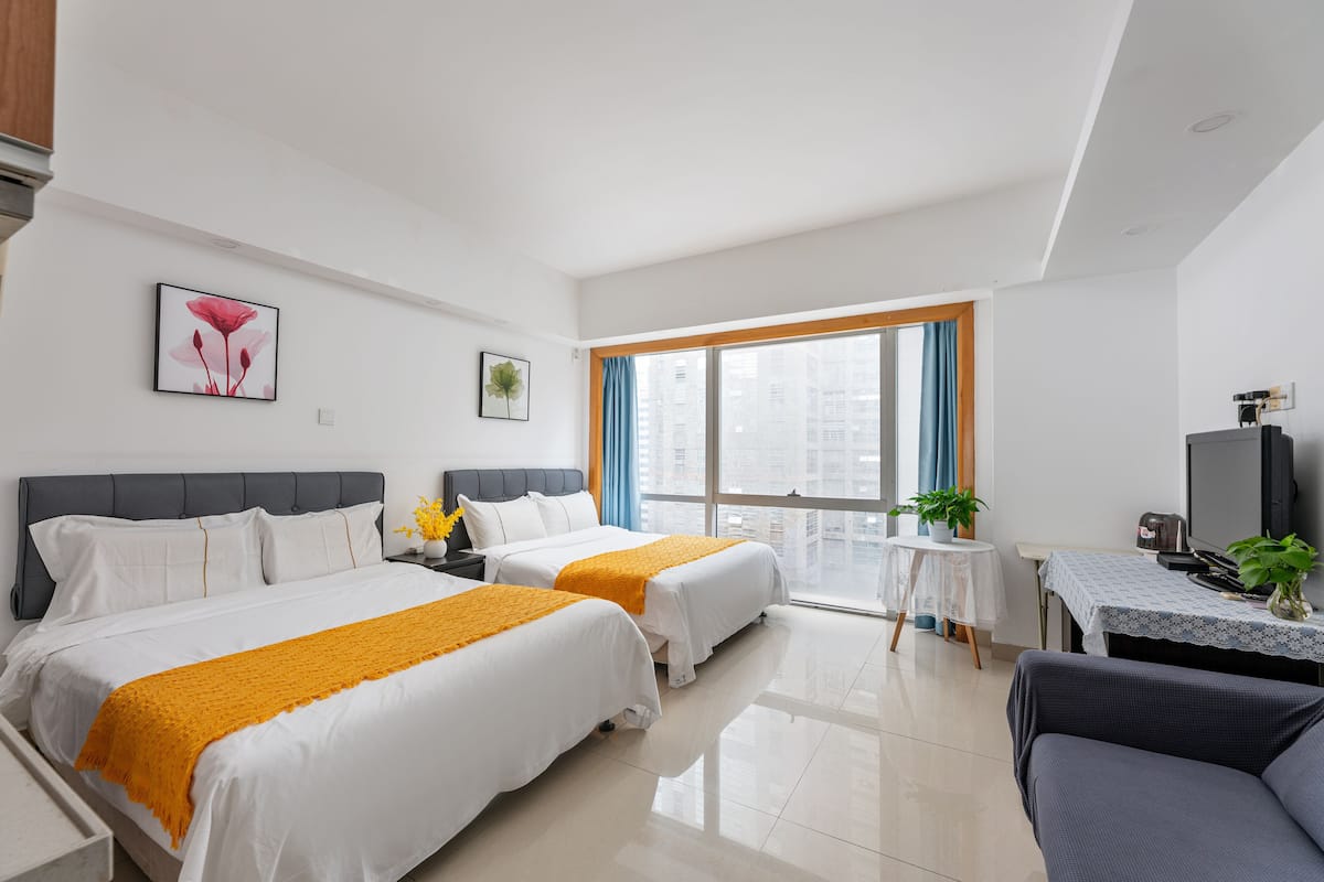 Quarto de hotel moderno com duas camas, um sofá, uma TV e uma varanda com vista para a cidade.