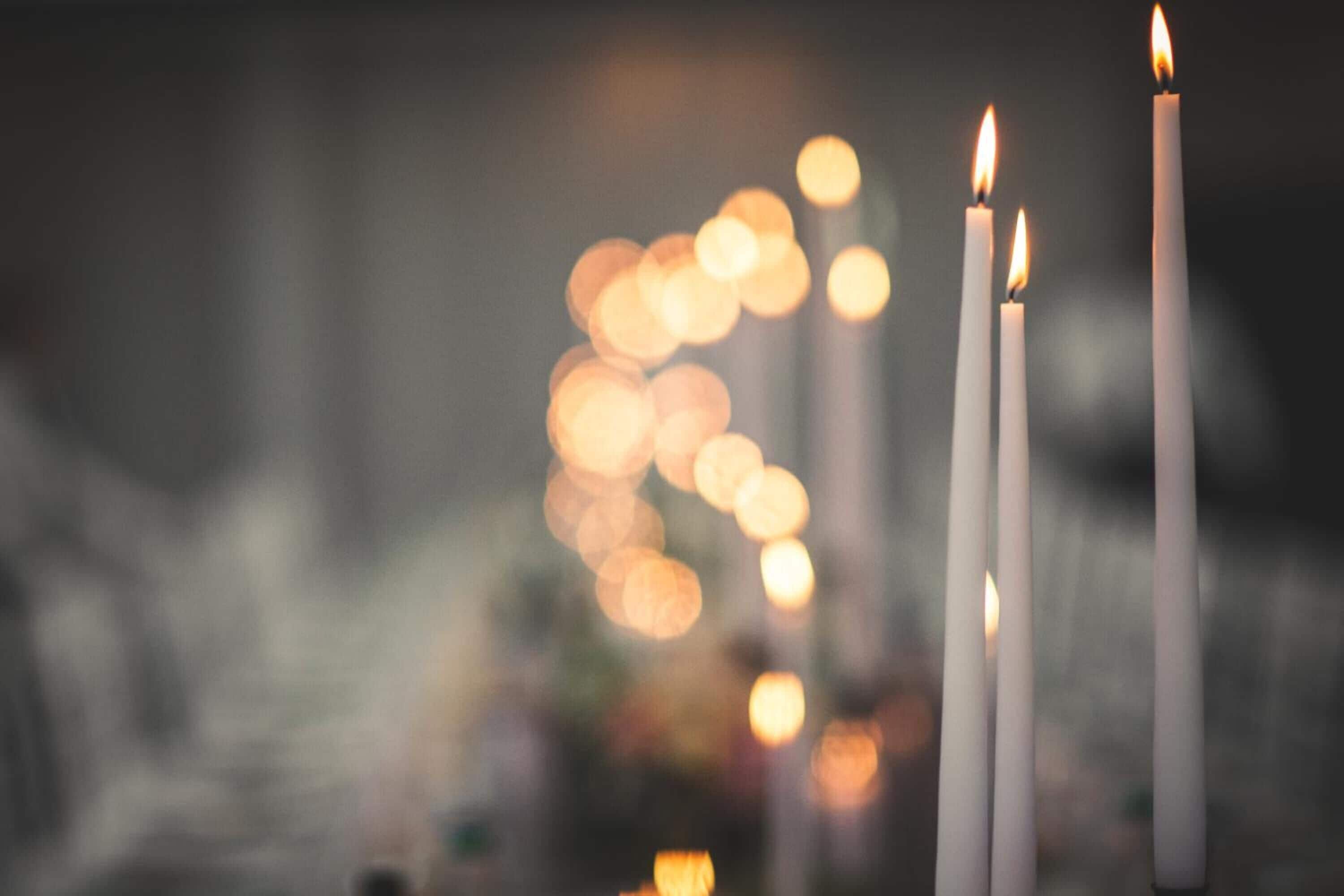 Várias velas brancas acesas, com chamas, em frente a um fundo desfocado com efeito bokeh.