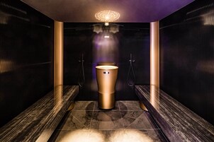 Um corredor moderno, com iluminação suave, apresentando uma estrutura cilíndrica central iluminada, com paredes escuras e texturizadas, e piso de pedra polida.