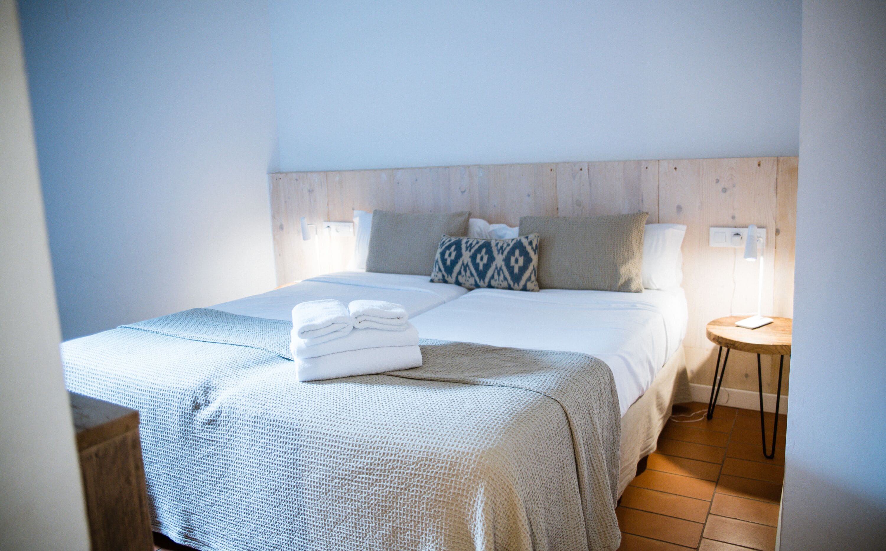 Uma cama bem arrumada com toalhas dobradas, uma cabeceira de madeira e uma mesa de cabeceira com uma luminária.