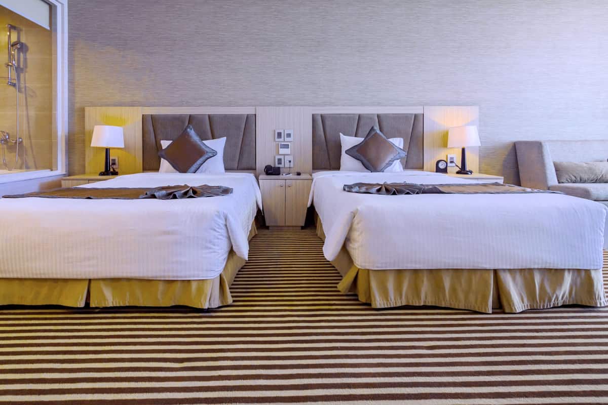 Quarto de hotel com duas camas, um sofá, uma mesa pequena e banheiro com chuveiro.