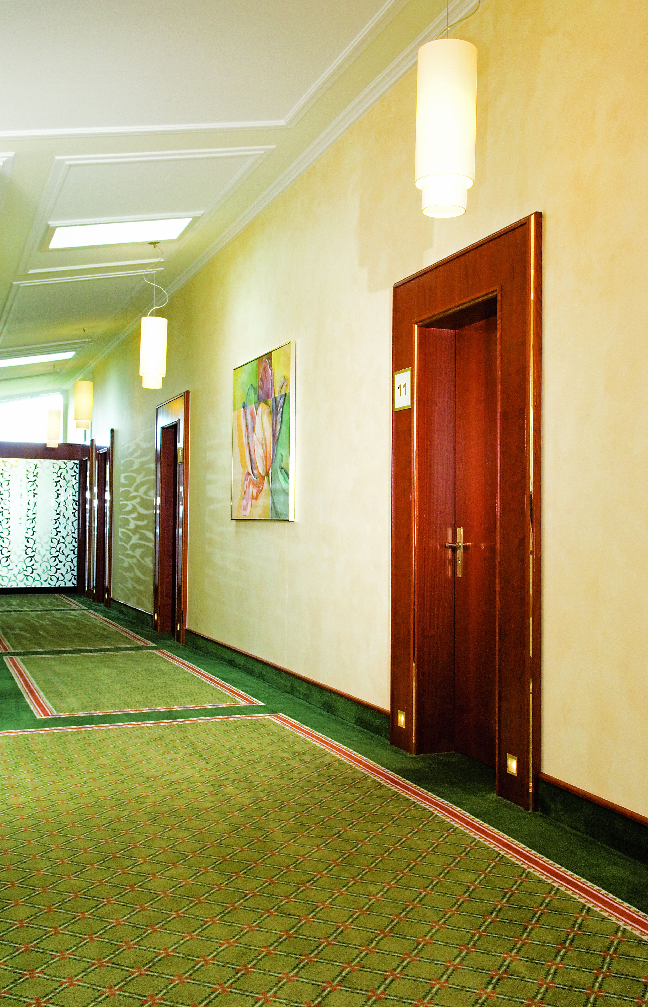 Um corredor de hotel com piso coberto por carpete, portas de madeira e um quadro na parede.