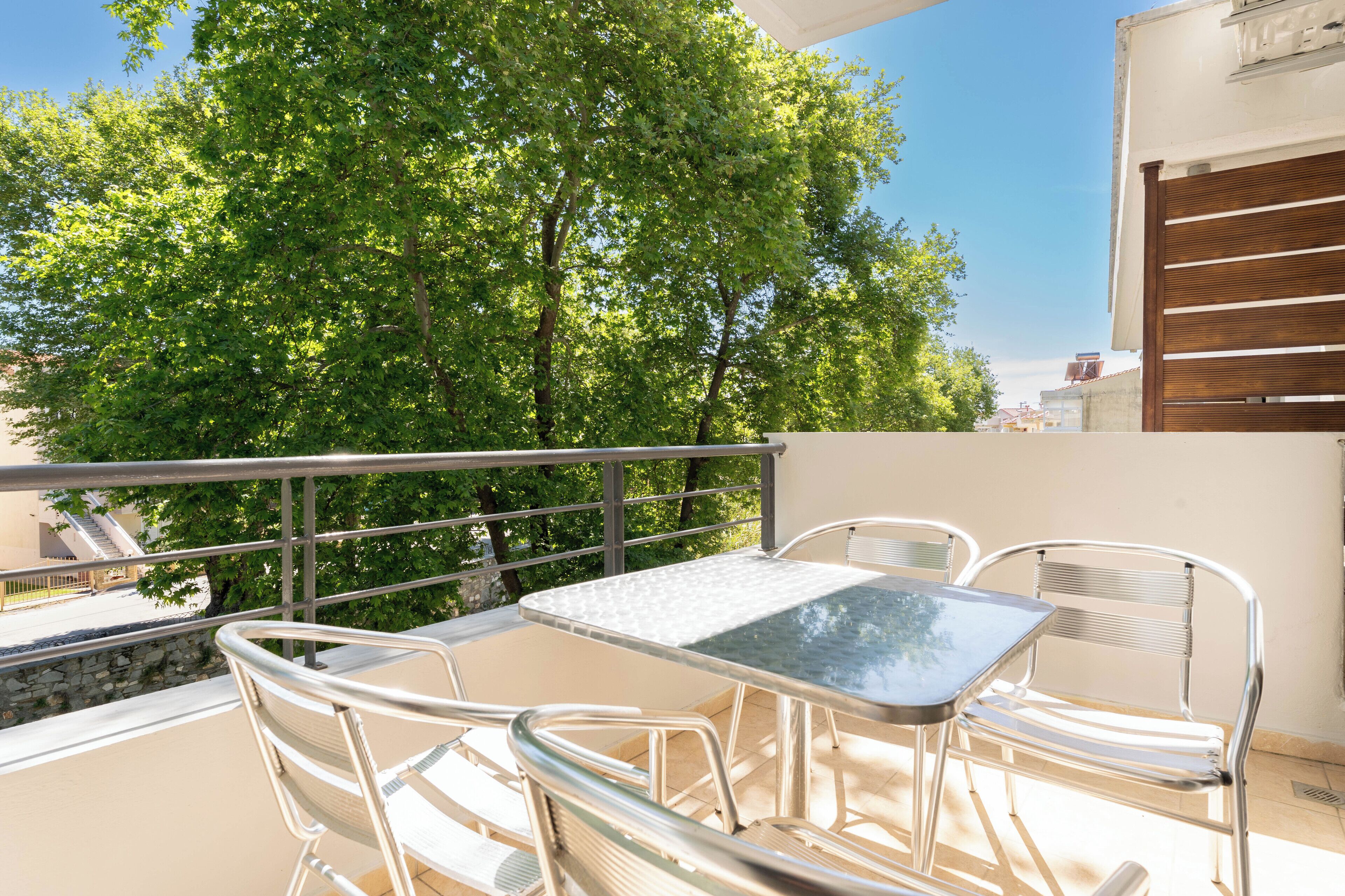 Varanda com mesa e cadeiras, com vista para um muro de pedra e árvores.