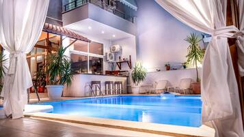 Piscina interior com área de bar, assentos e plantas em vasos.