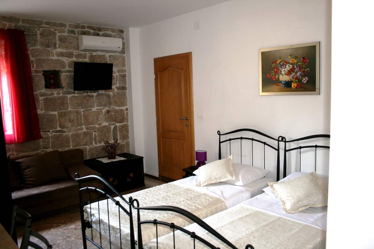 Um quarto com parede de pedra, cama com roupa de cama branca, porta de madeira e um quadro na parede.