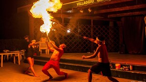 Espetáculo noturno ao ar livre com apresentações de fogo em frente a um edifício com a inscrição 'VILLAGGIO CAMPING'.