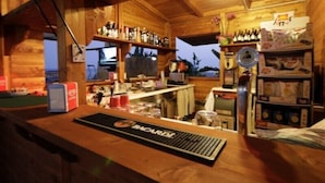 Área de bar com paredes de madeira, um balcão com minibar e prateleiras repletas de garrafas.