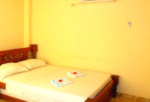 Uma cama de solteiro com cabeceira de madeira, colchão branco e duas toalhas listradas sobre a cama.