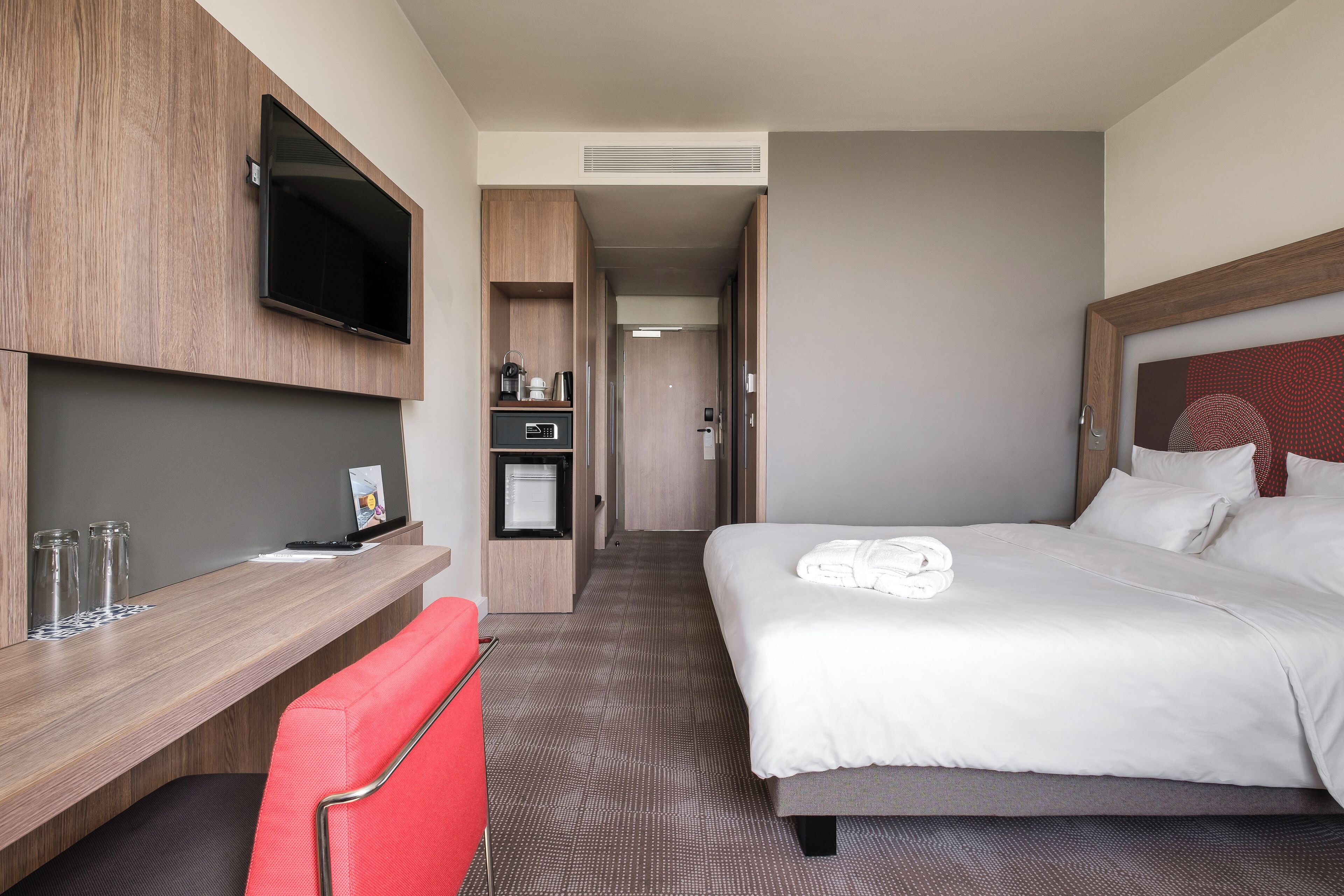 Quarto de hotel com uma cama, uma mesa, uma televisão e uma cadeira vermelha.