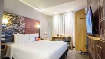 Quarto de hotel com uma cama grande, uma escrivaninha com cadeira, uma televisão e TV fixada na parede.
