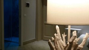Quarto com abajur moderno, escultura de madeira e porta para uma área pouco iluminada.