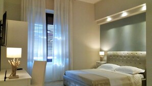 Quarto de hotel com uma cama grande, uma escrivaninha com abajur e uma cadeira.
