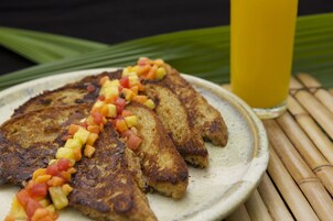 Um prato de sanduíches grelhados com fruta picada sobre um prato de cerâmica, acompanhado por um copo de suco de laranja.