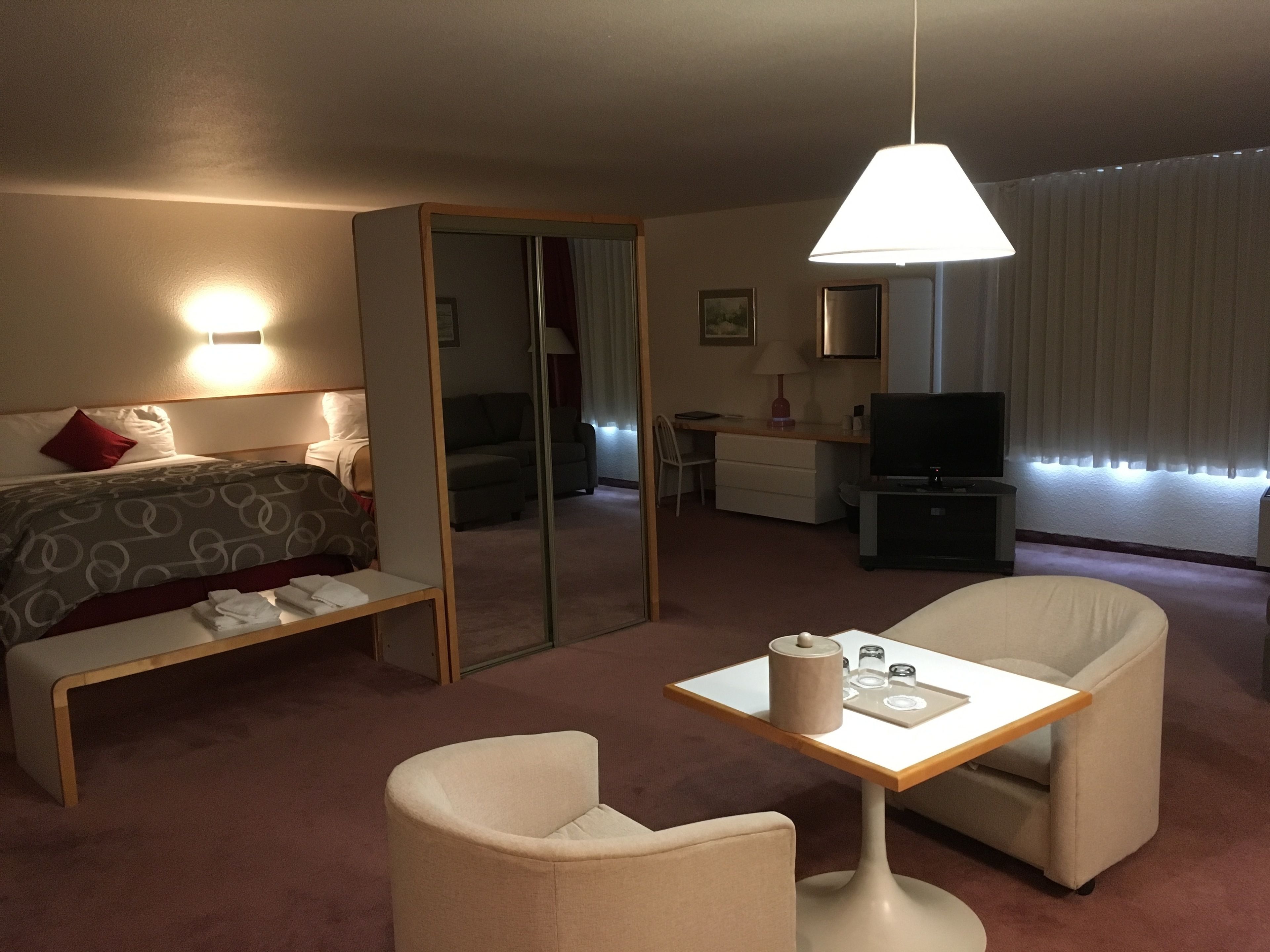 Quarto de hotel com cama, escrivaninha com televisão, sofá e poltrona.