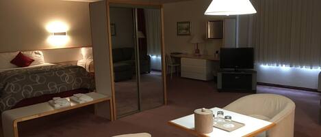 Quarto de hotel com cama, escrivaninha com televisão, sofá e poltrona.
