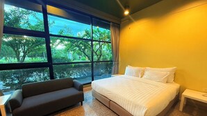 Quarto com cama, sofá e uma janela grande que oferece vista para árvores e um edifício.