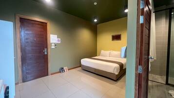 Quarto de hotel com cama, porta, luminária na parede e piso de azulejos.