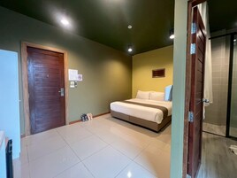 Quarto de hotel com cama, porta, luminária na parede e piso de azulejos.