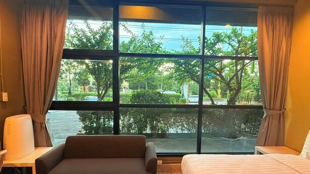 Quarto de hotel com uma janela grande, um sofá, uma cama e uma escrivaninha com abajur.