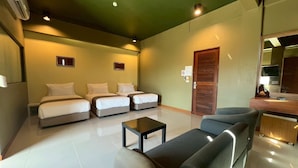 Quarto de hotel com uma cama grande, duas camas menores, um sofá, uma mesa de centro e uma porta de madeira.