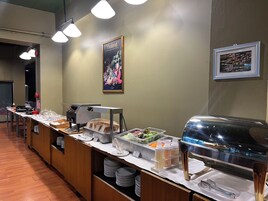 Disposição de buffet com diversos alimentos e acompanhamentos, pôster da Tailândia e uma moldura na parede.